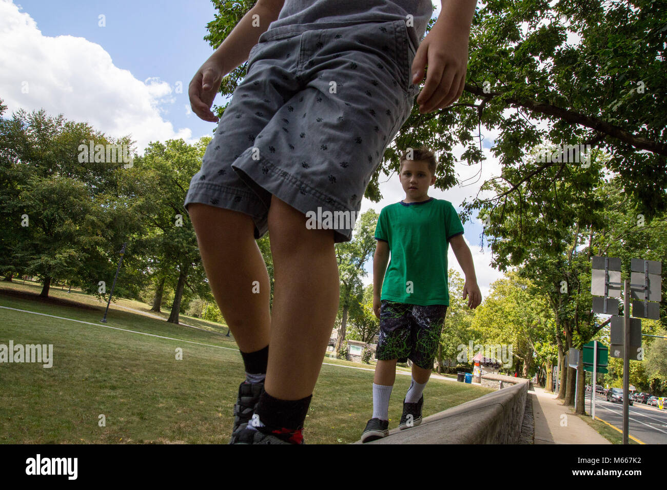 Twin Caucasian brothers walk single file on top of a rock wall next to ...