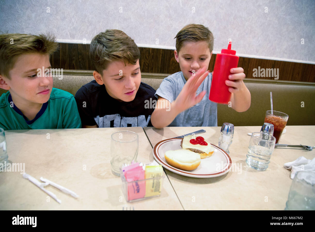 Two Twin and One Older Caucasian Brother Sit and Eat a Hamburger at an ...