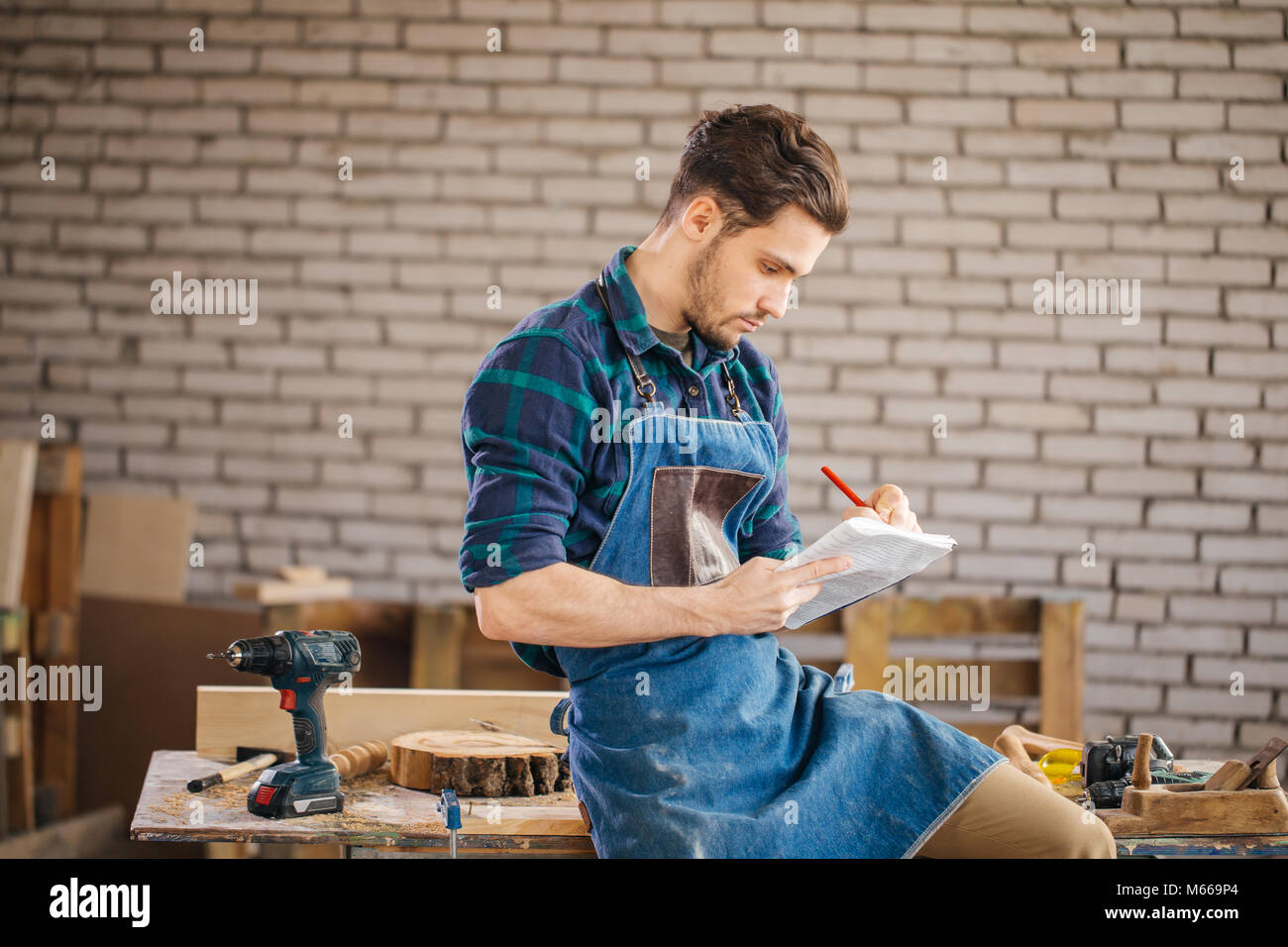 Man carpenter in his home studio draws sketches in pencil in notebook ...
