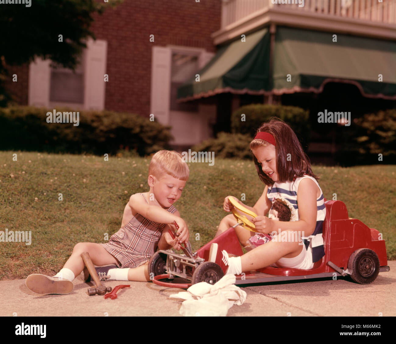 1960s GIRL SITTING IN RED TOY CAR ON SIDEWALK BOY PLAYING MECHANIC ...