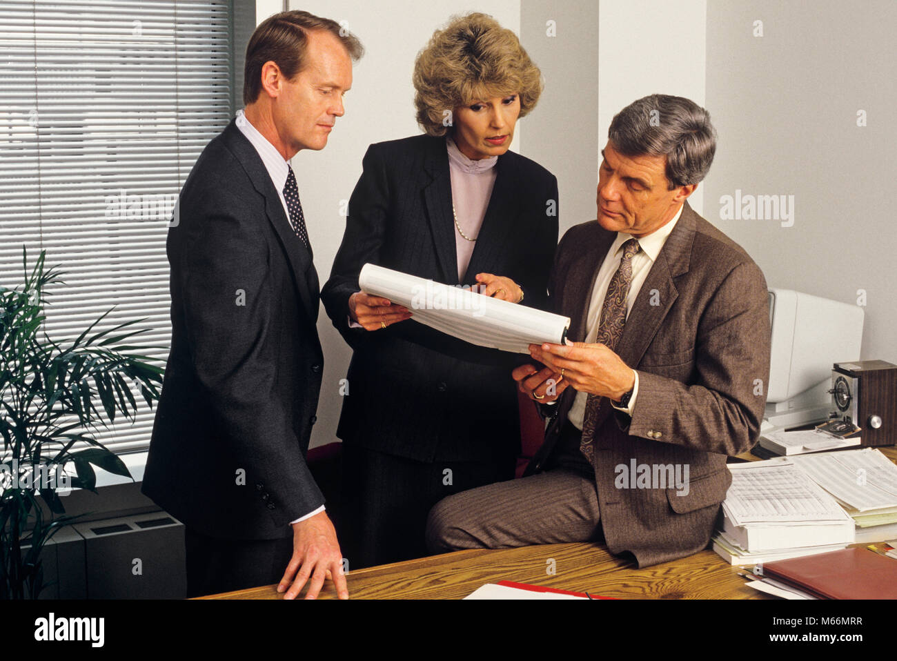 1980s 3 EXECUTIVES HOLDING MEETING IN OFFICE REVIEWING PAPER WORK ...