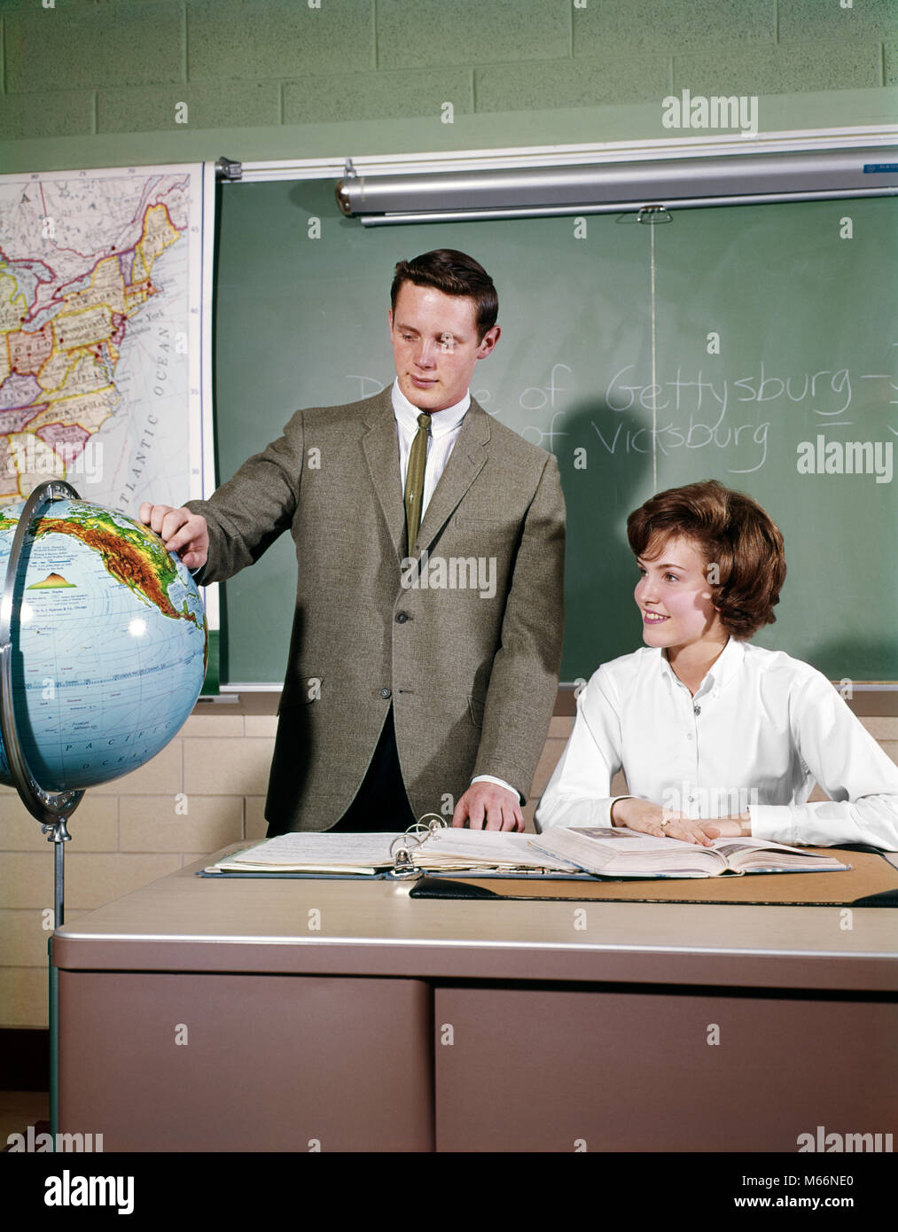 1960s 2 STUDENTS IN CLASSROOM TEEN BOY STAND BY GLOBE GIRL SEATED AT ...