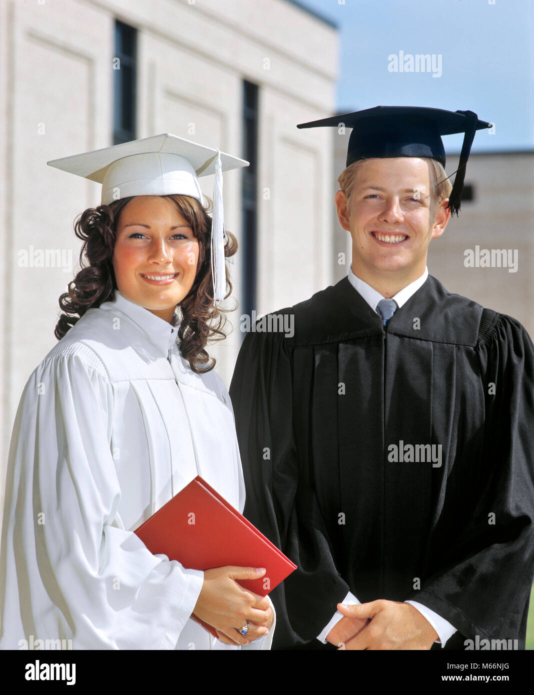 1970s PORTRAIT STUDENT COUPLE IN GRADUATION ROBES LOOKING AT CAMERA ...