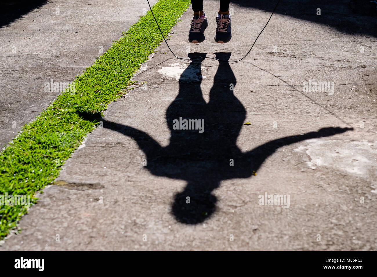 shadow of fit woman with black clothing jumping rope in the park under ...