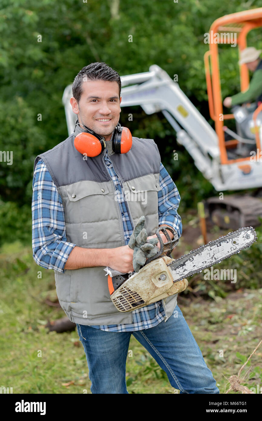 Man holding chainsaw, digger in background Stock Photo - Alamy