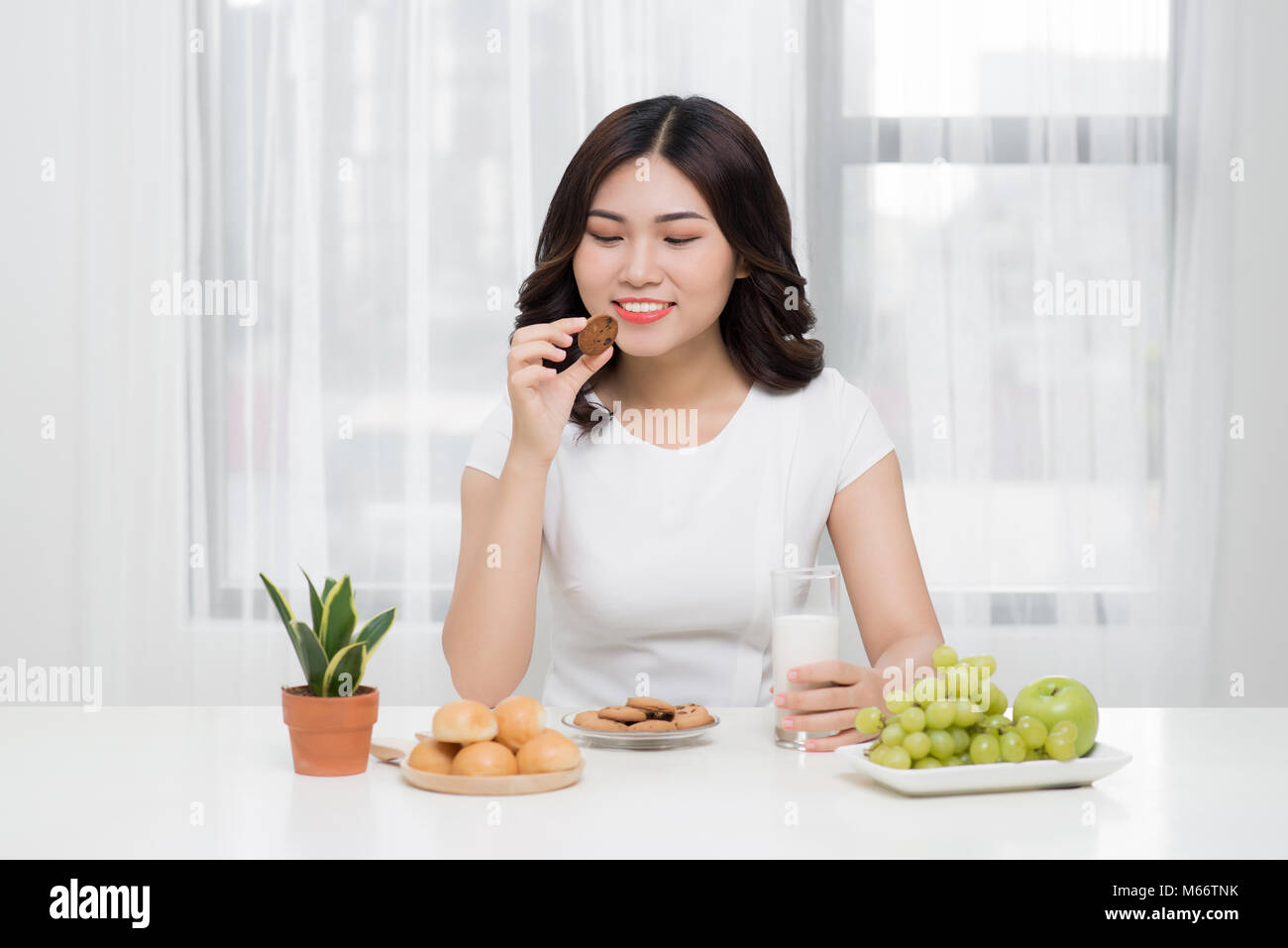 Pretty young asian woman eating tasty cookie at home Stock Photo - Alamy