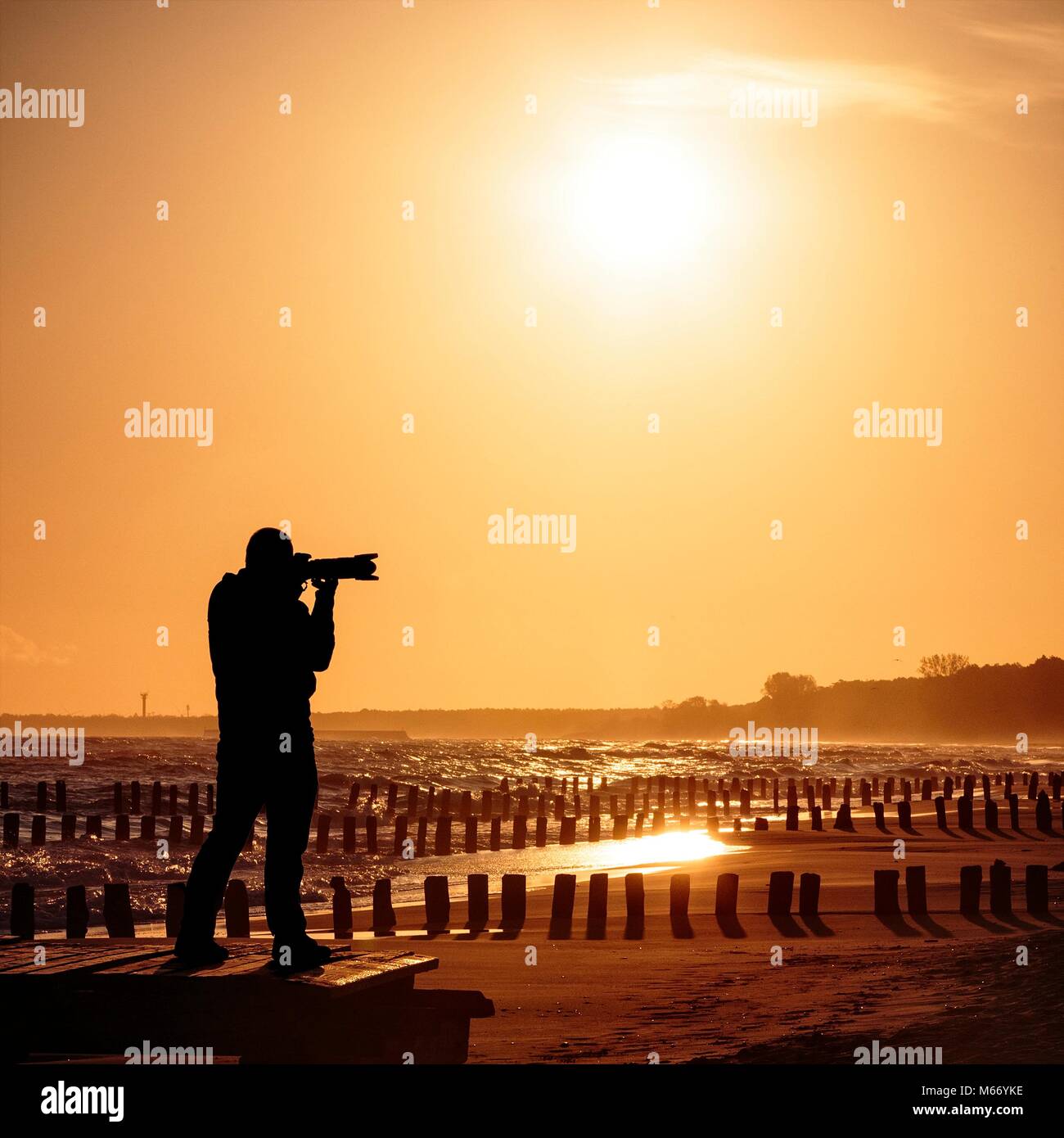 Silhouette of standing photographer on the golden beach during sunrise ...