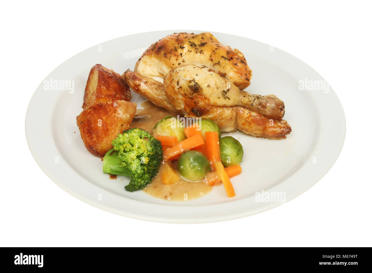 Roasted poussin chicken with roast potatoes vegetables and gravy on a ...
