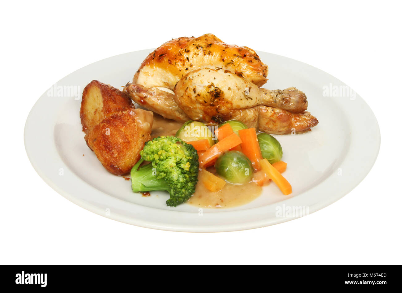 Roasted poussin with vegetables and gravy on a plate isolated against ...