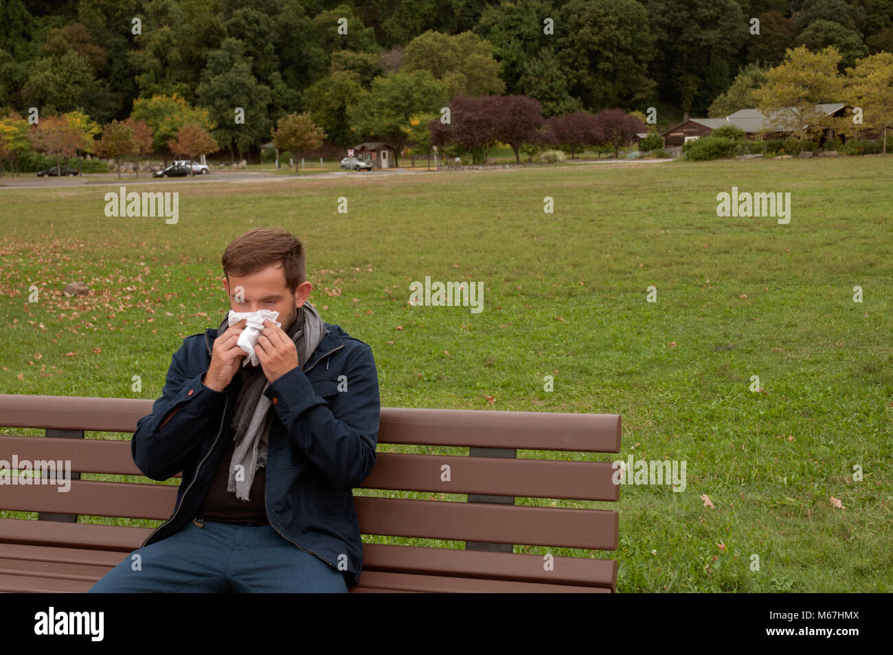 Man has cold or flu. Man has catch cold is sitting on bench in the park ...