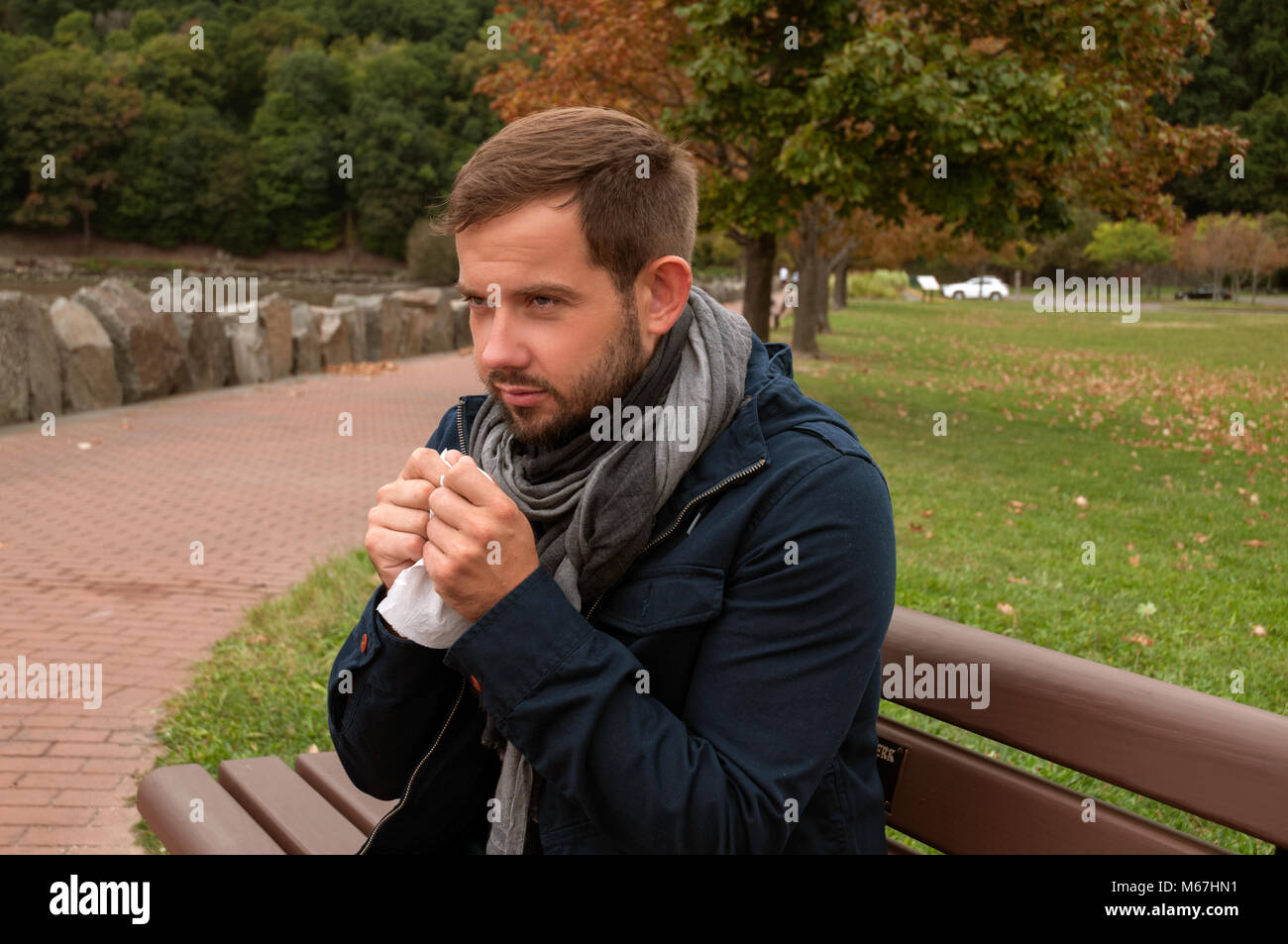 Man has cold or flu. Man has catch cold is sitting on bench in the park ...