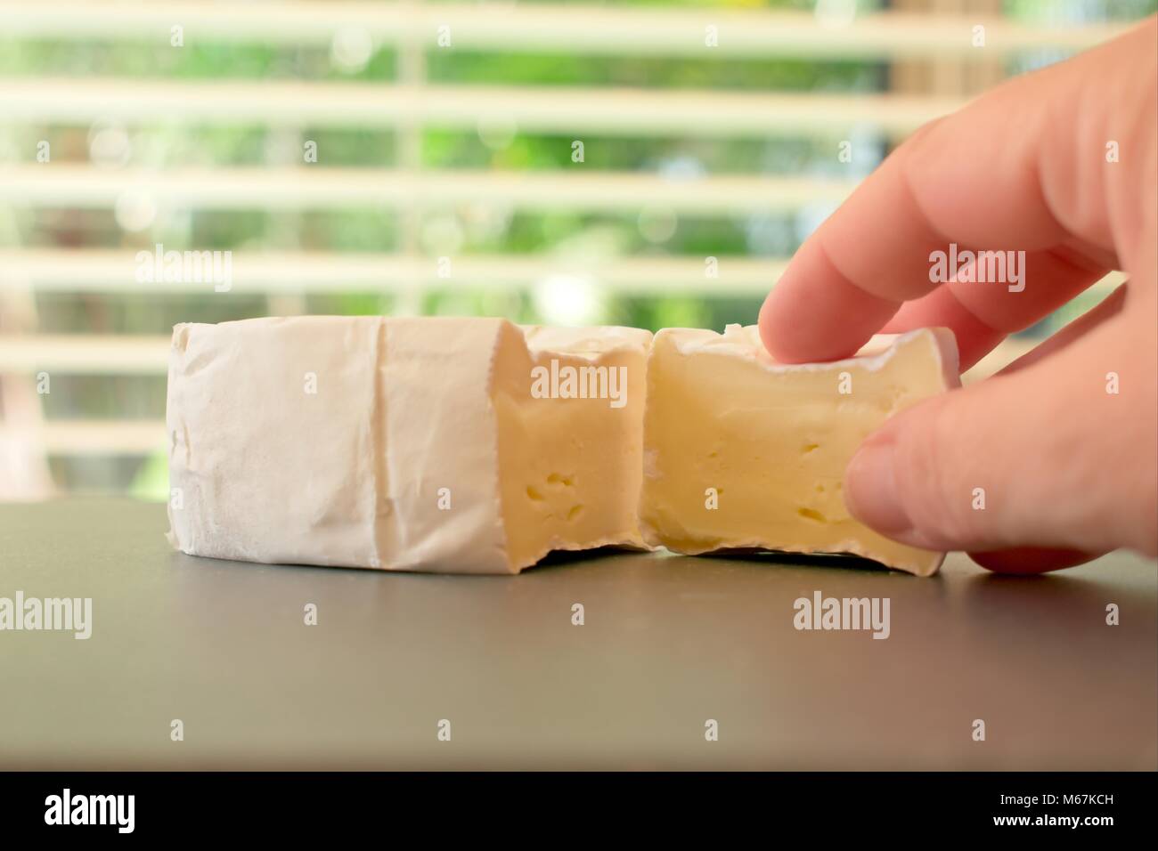 Hand grabbing a piece of camembert cheese Stock Photo - Alamy