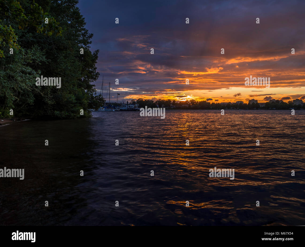 sunset on a lake with forest on the left side Stock Photo - Alamy