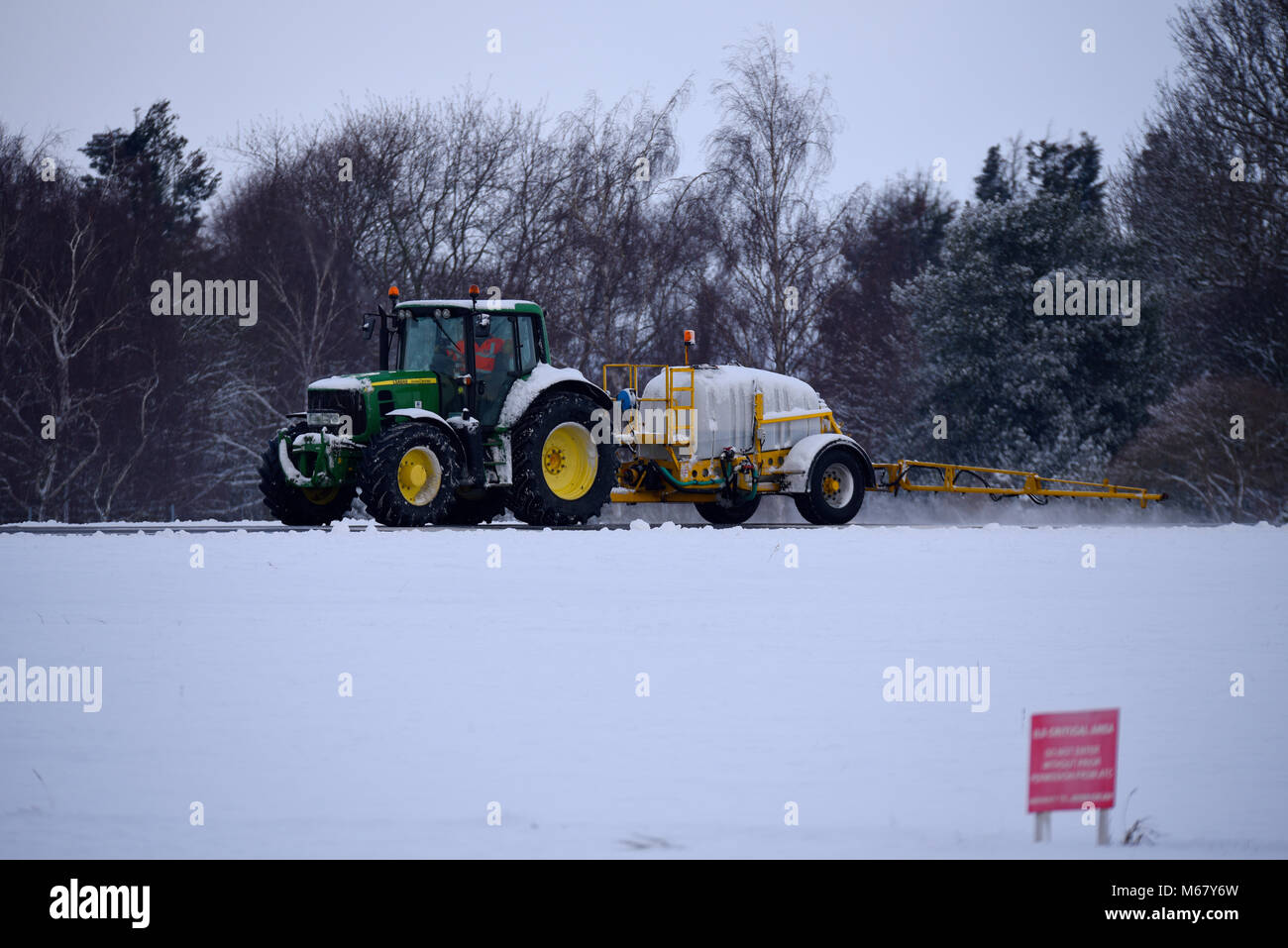 Airport runway snow clearing. John Deere Tractor pulling a de-icing ...