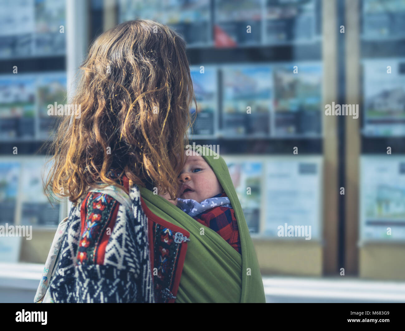 A young mother is looking at an estate agent's window with her baby in ...