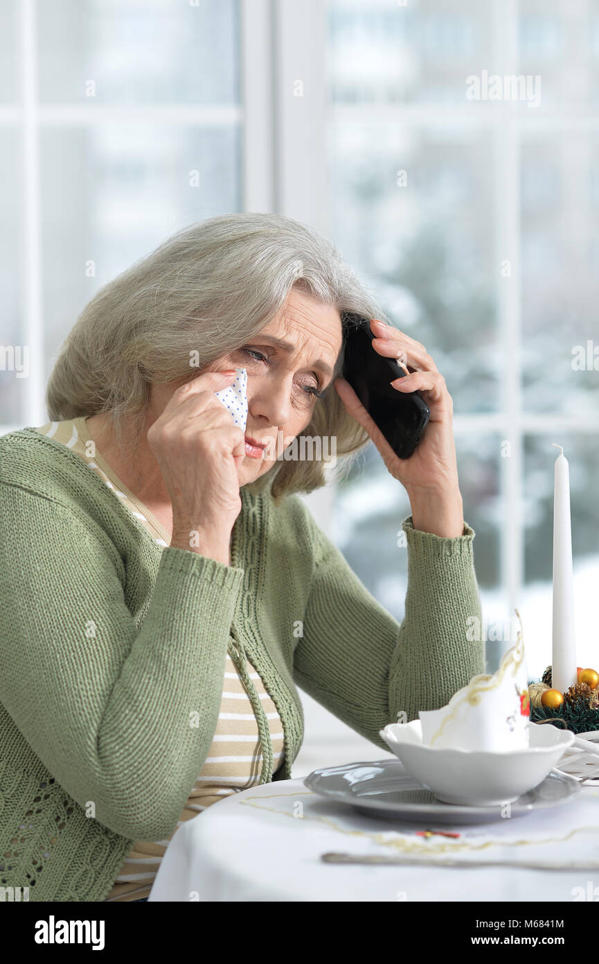 sad woman sitting at table with phone Stock Photo - Alamy