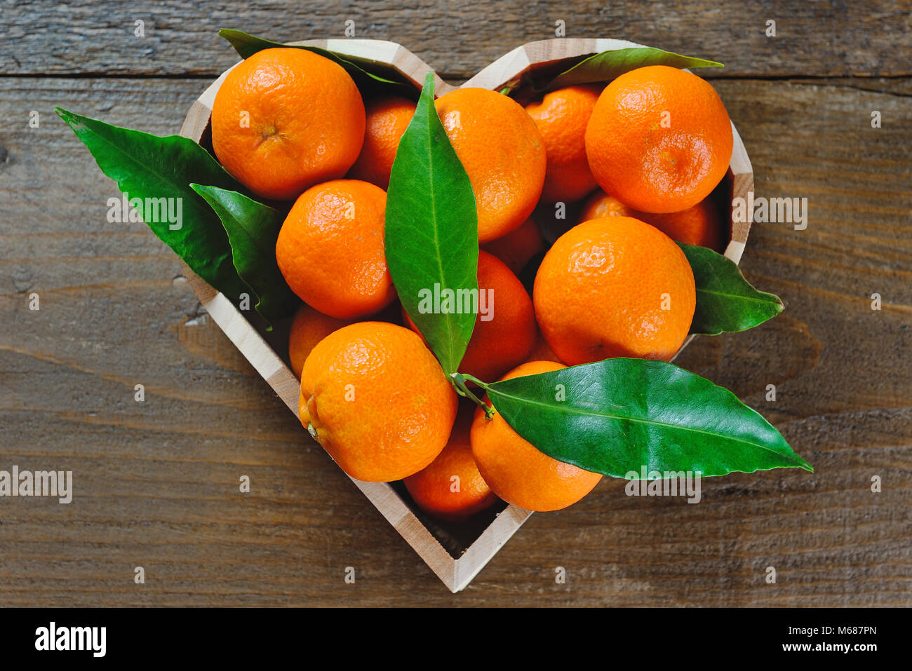 Fresh clementine in a heart shaped box on a brown wooden background ...