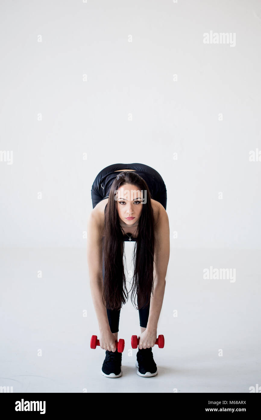 The front view of the pretty sportwoman bending with the red dumbbells ...