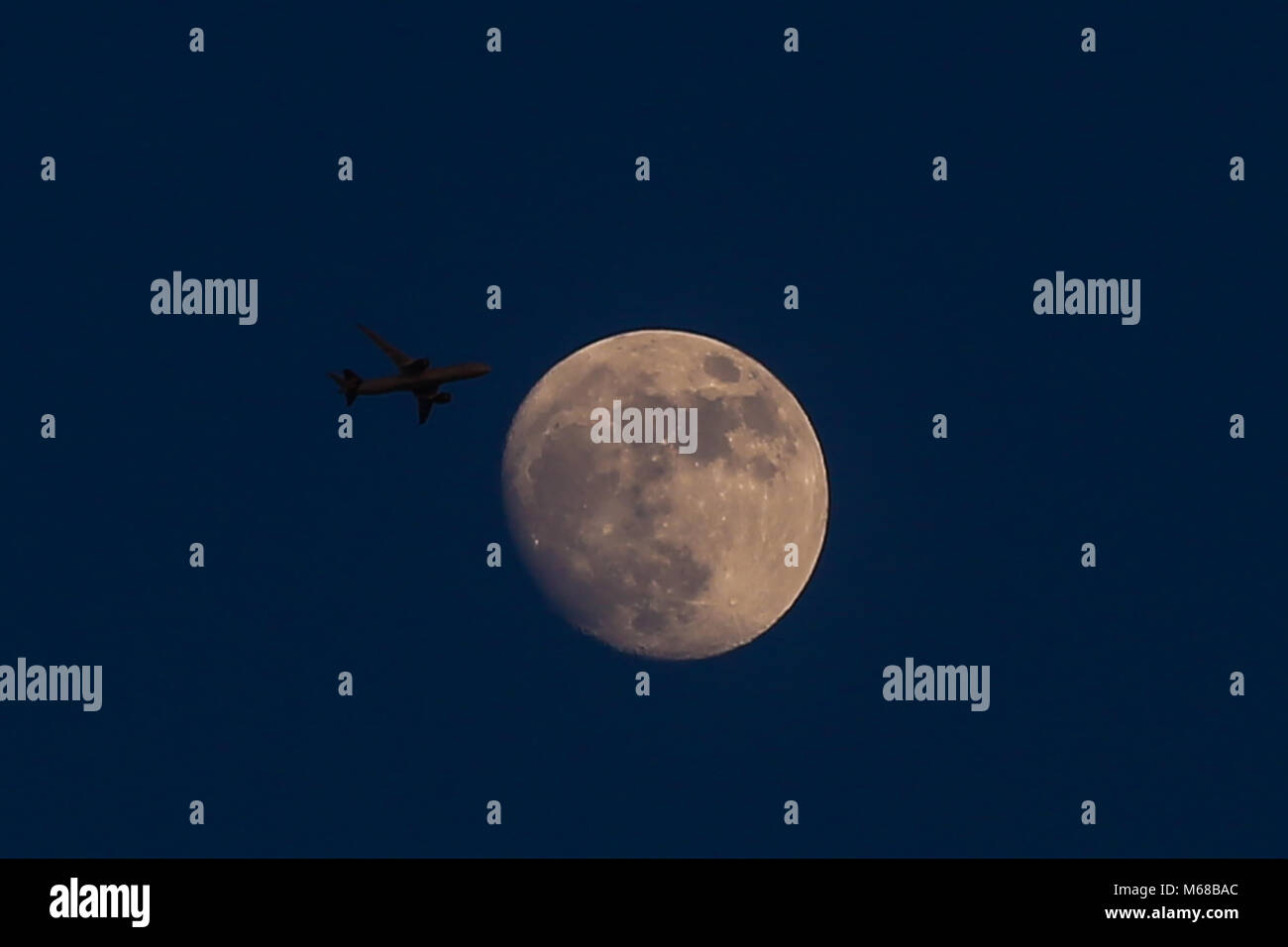 A plane flies in front of nearly full moon over north London. Featuring ...