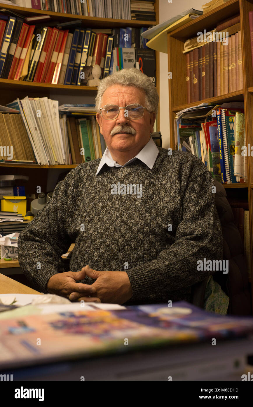 a retired older man sits at his desk in his home office with files and ...