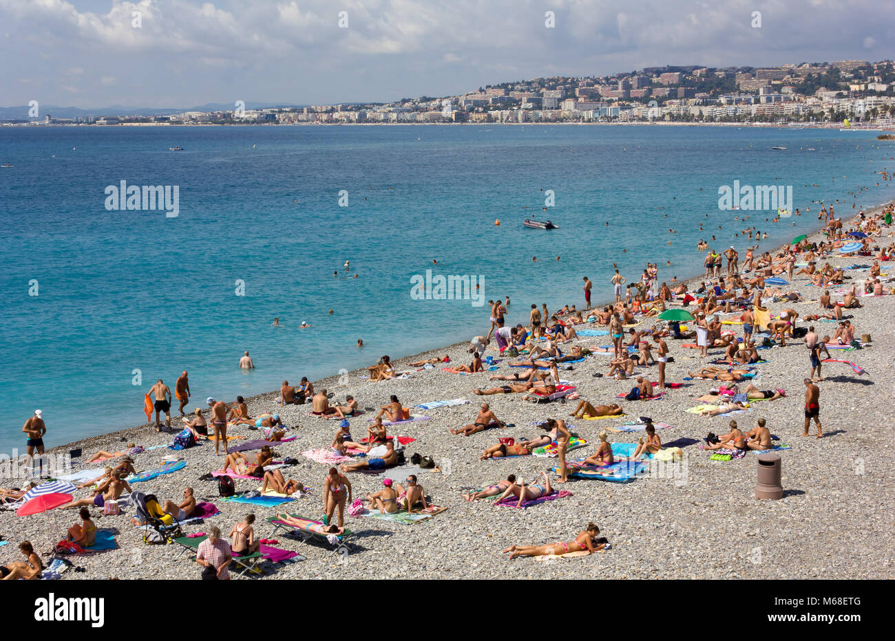 Crowded pebble beach in Nice, France, in front of a turquoise blue sea ...