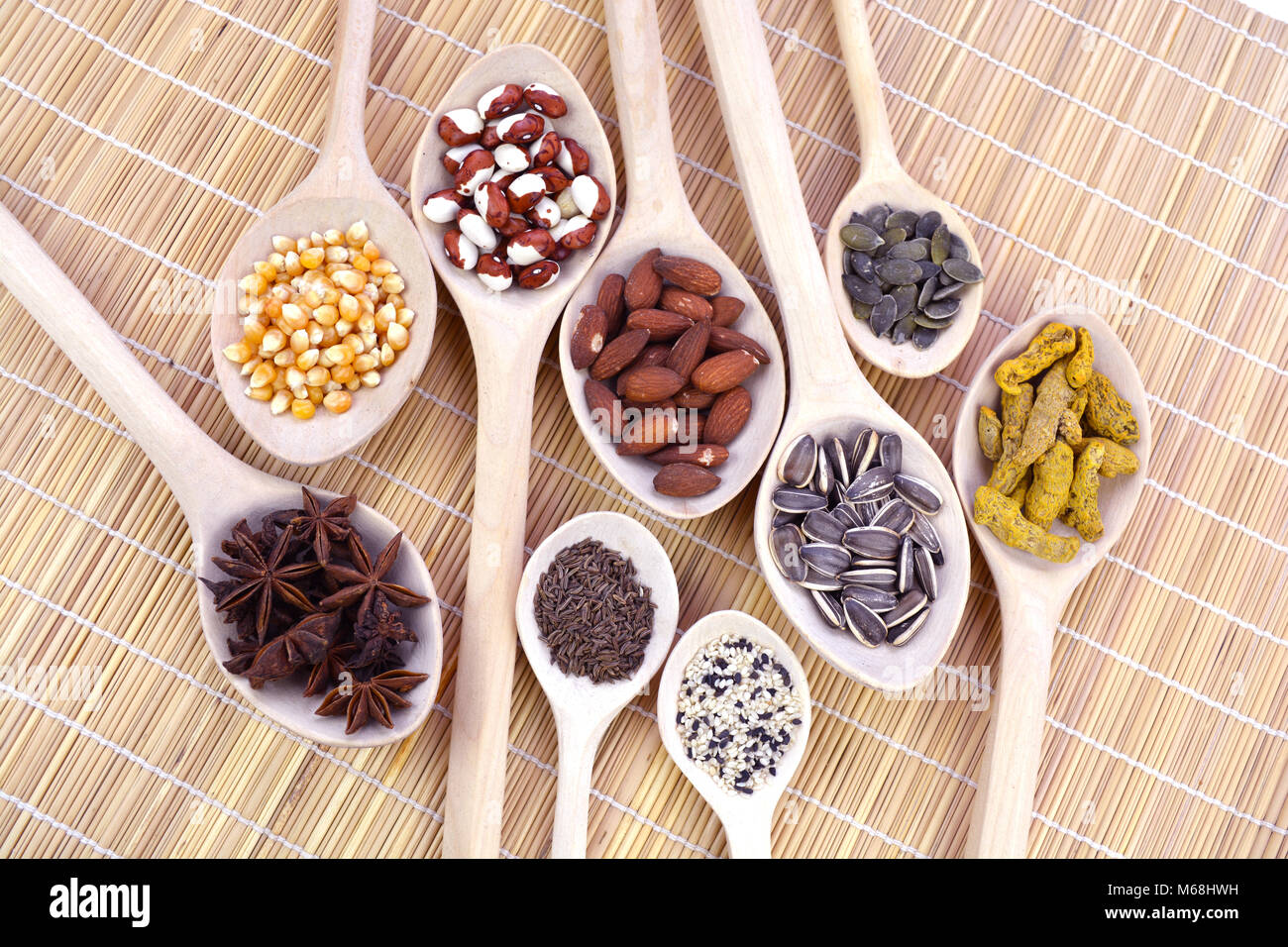 Nine wooden spoons on bamboo mat with healthy seeds, nuts and spices ...