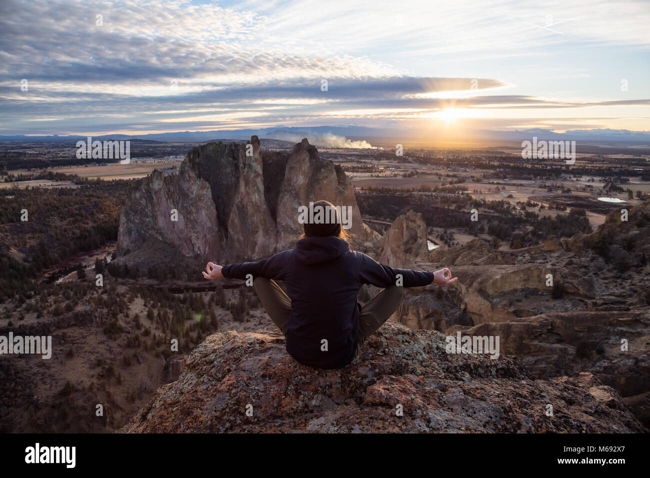 Adventurous man sitting in a meditation pose on top of a cliff during a ...