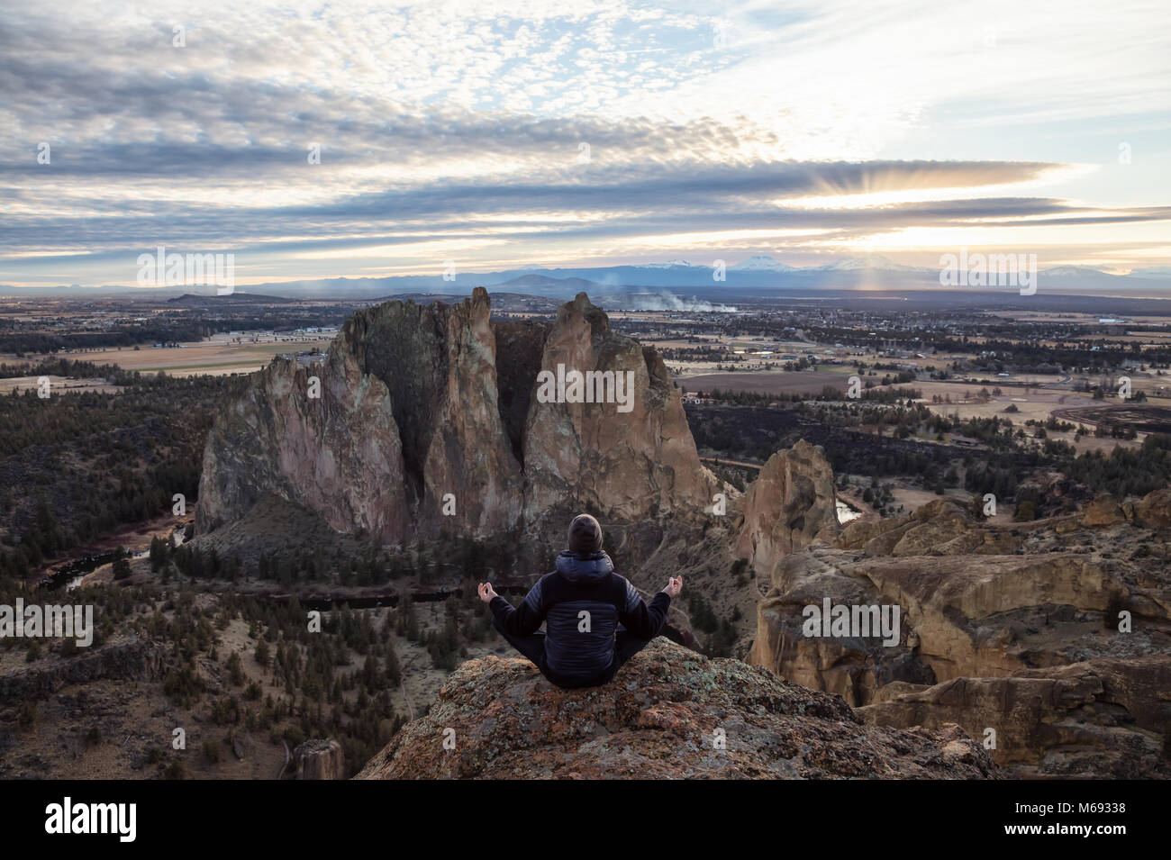 Adventurous man sitting in a meditation pose on top of a cliff during a ...