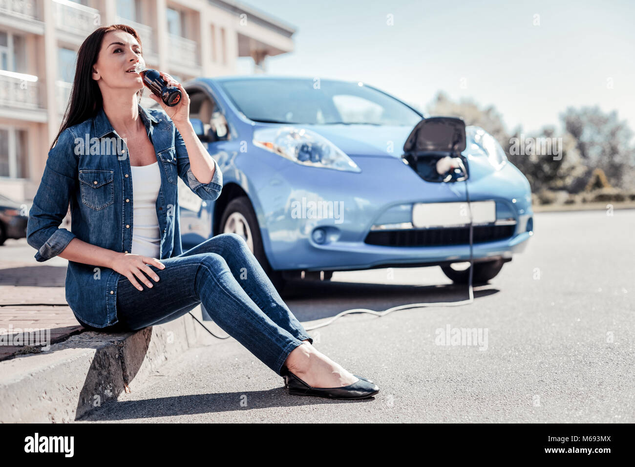 Young cute woman charging the car drinking cola Stock Photo - Alamy