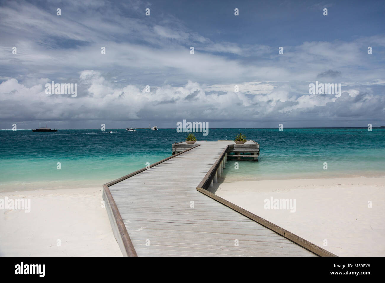 small wooden jetty going out into a turquoise blue Maldivian Ocean on a ...