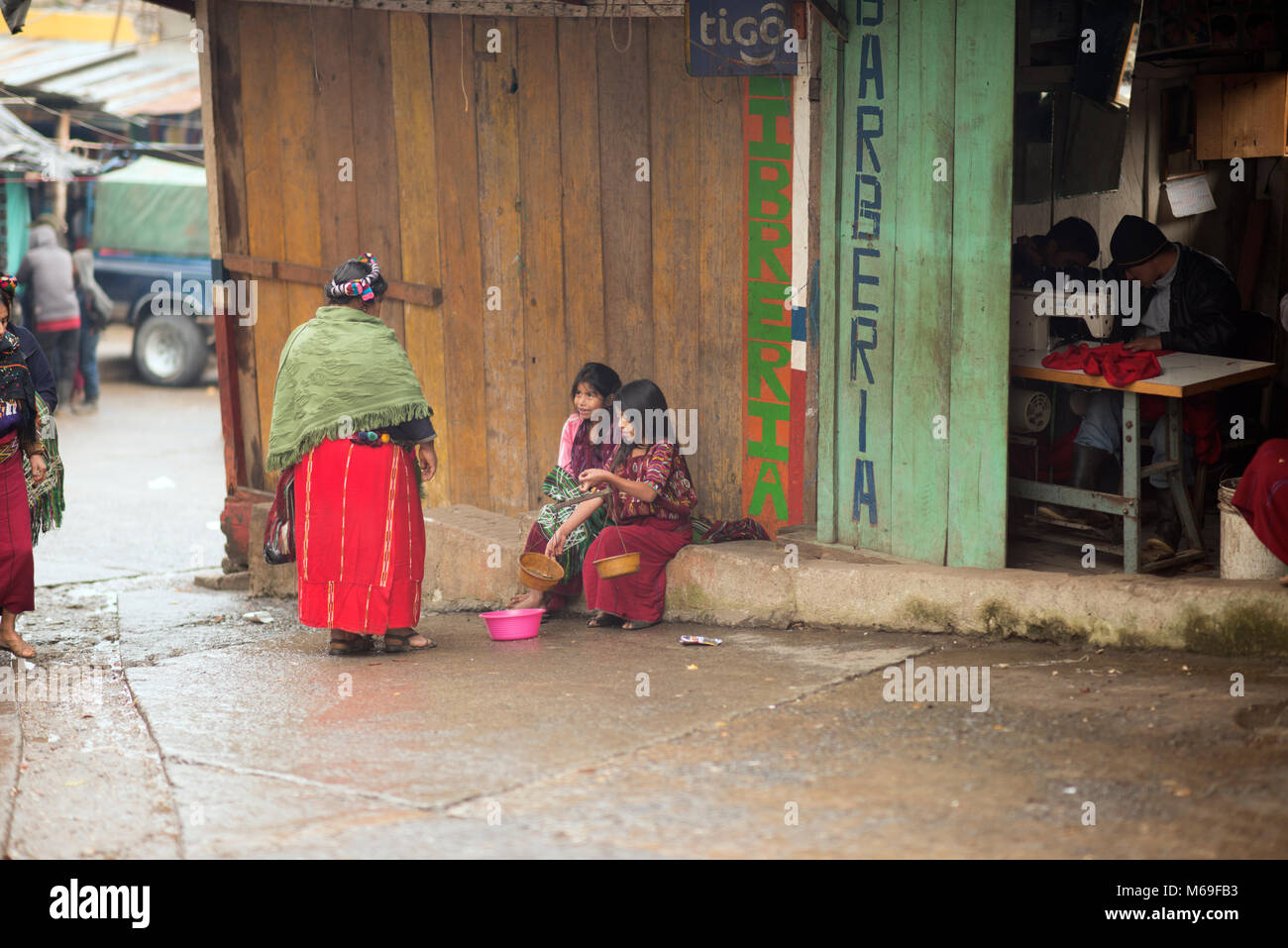 An indigenous, ethnic Ixil Maya woman stops to buy goods from two girls ...