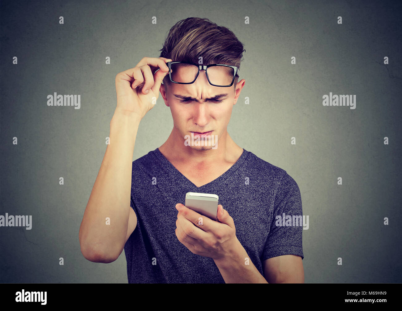 Casual confused young man in t-shirt and eyeglasses surfing smartphone ...