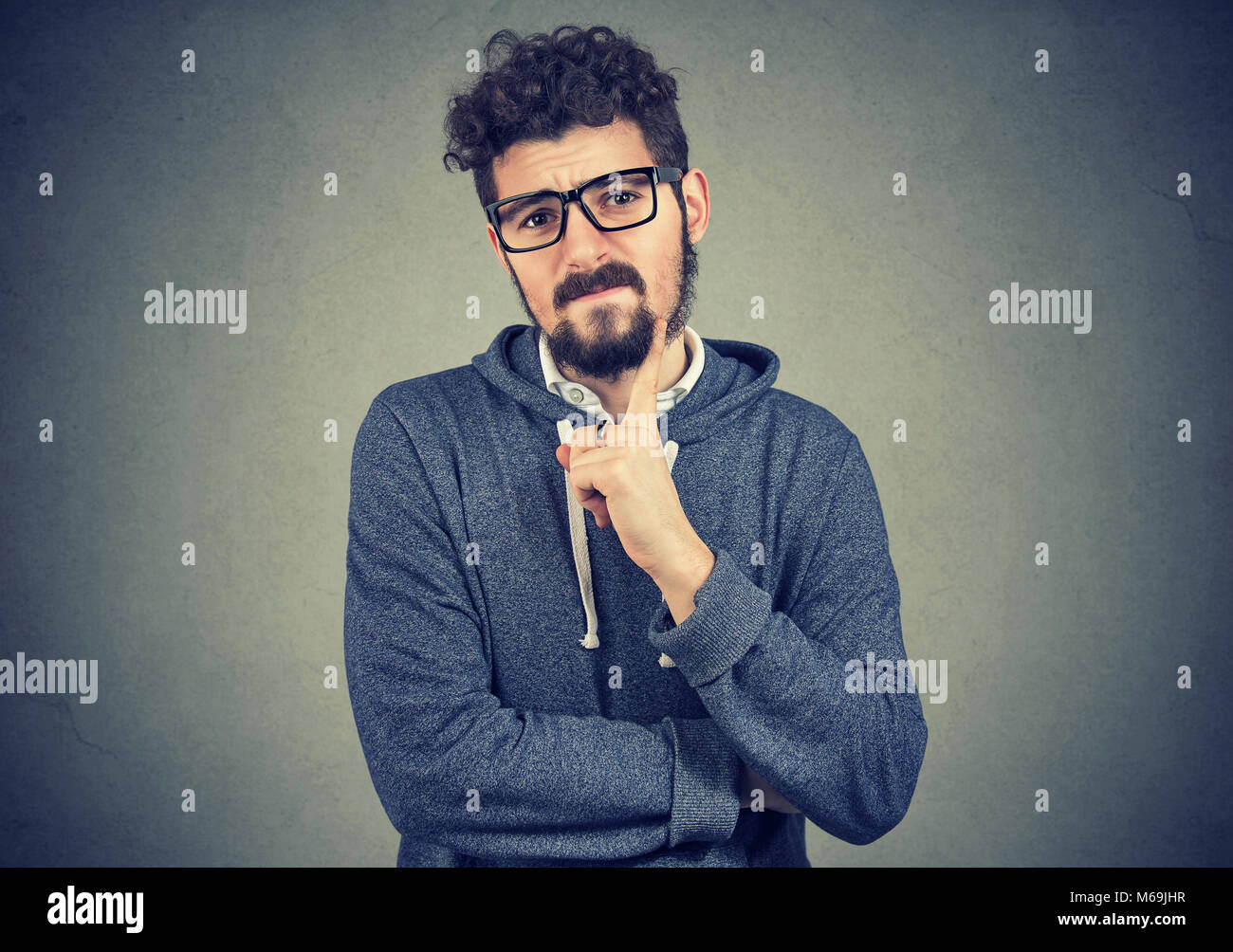 Young man with skeptic felling on face looking at camera on gray ...