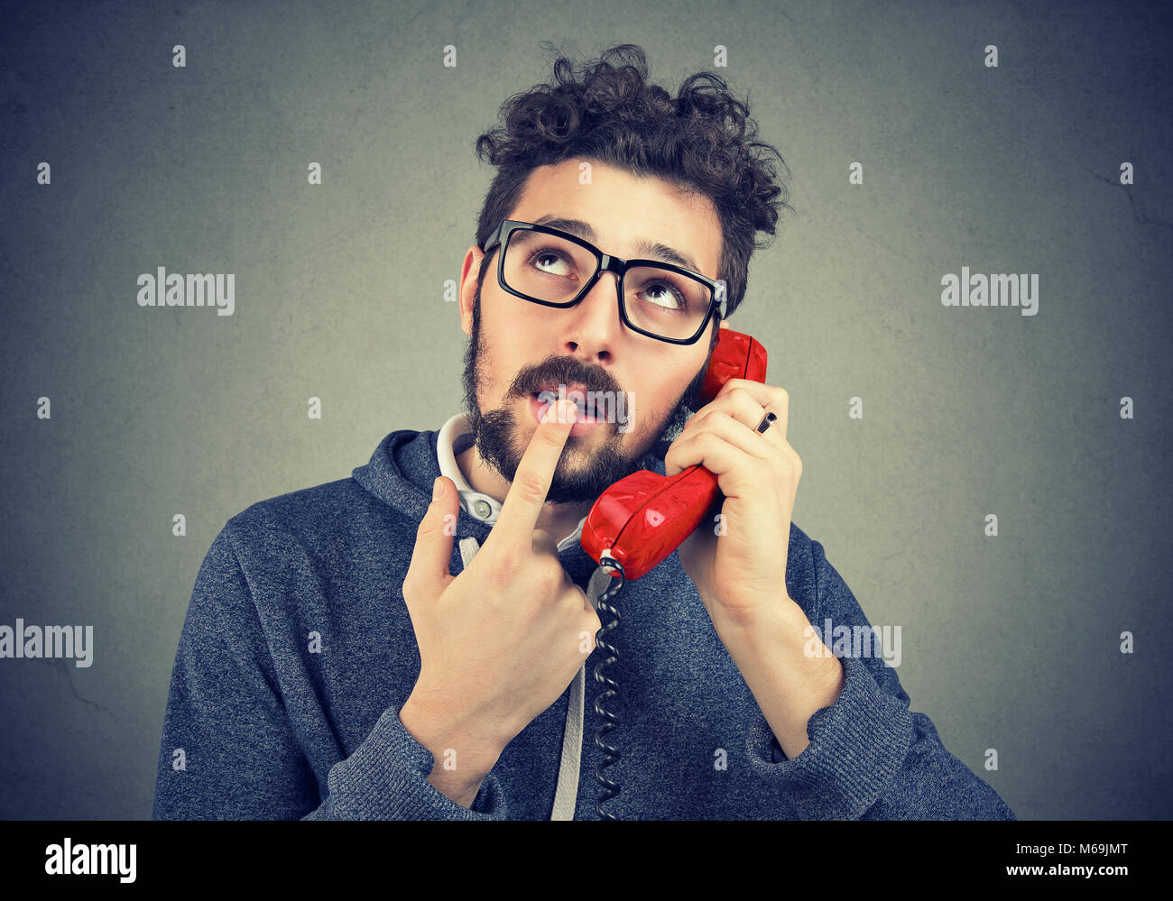 Young casual man looking up in confusion while talking on telephone ...