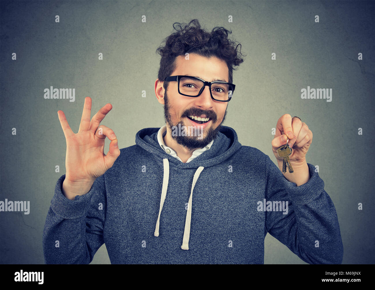 Young cheerful man showing OK gesture and boasting with keys from new ...