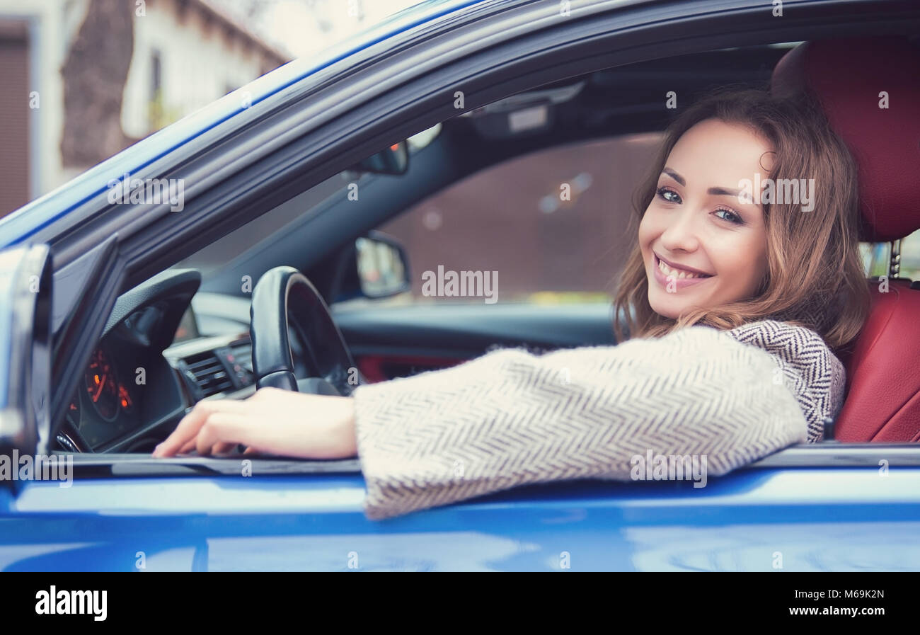 Young successful woman in coat sitting in personal car and driving ...