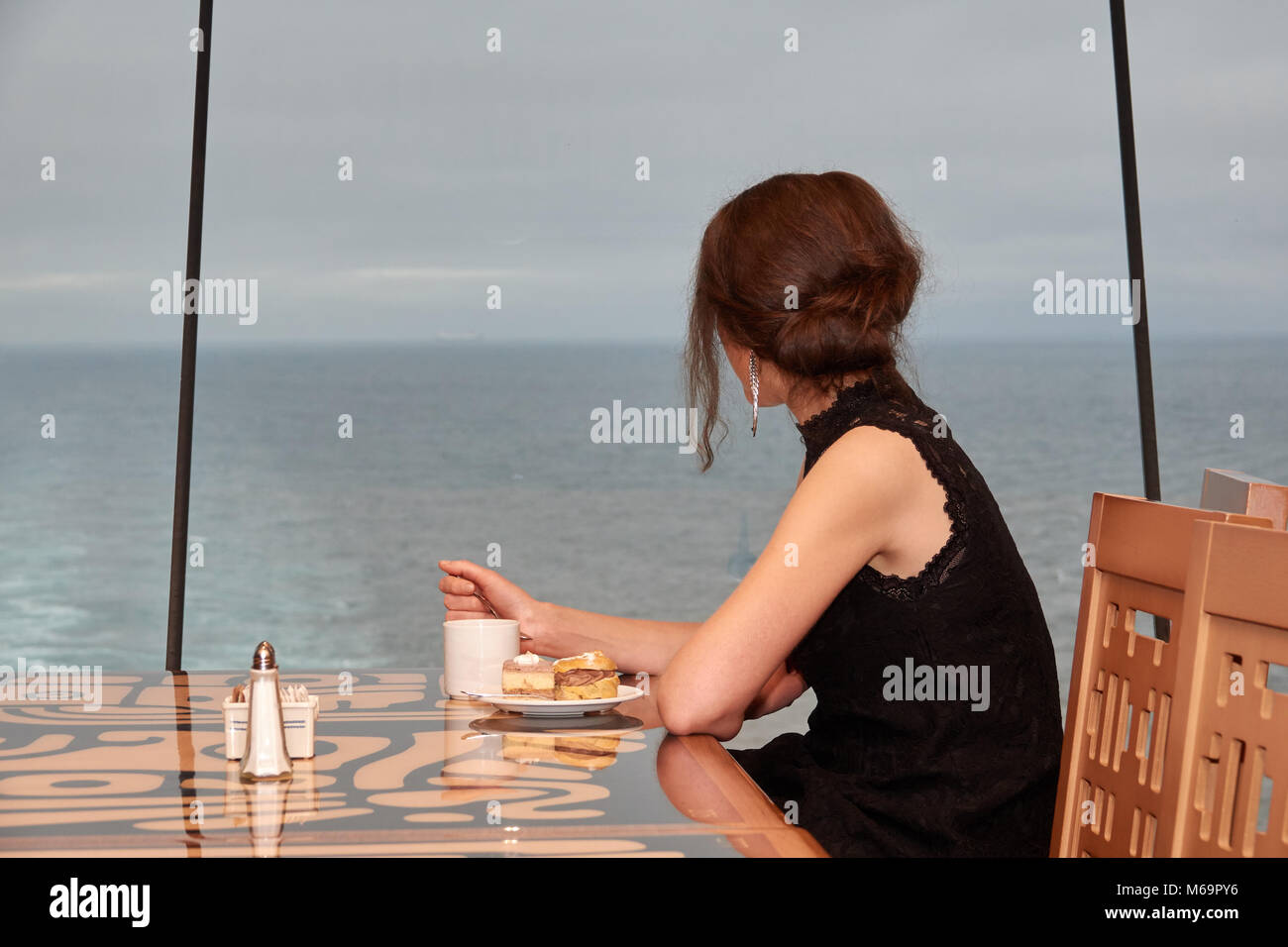 A girl in a cruise liner restaurant is eating a cake and looking out ...