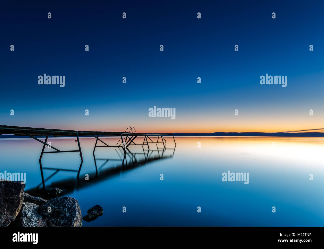 Long jetty with ladder in lake at sunrise Stock Photo - Alamy