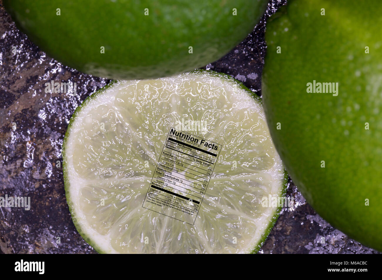 Close up of lime slice with fresh whole limes on granite with ...