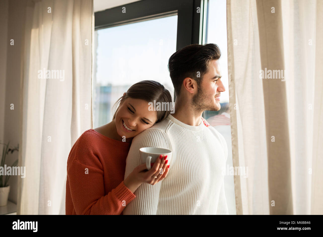 Portrait of happy woman with cup of coffee cuddling to her boyfriend ...