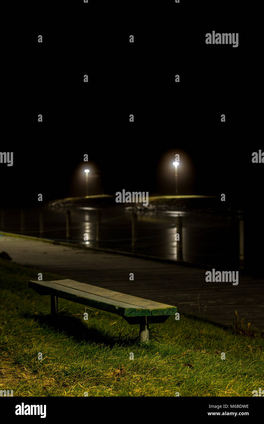 Nightphoto of bench with lights in background Stock Photo - Alamy