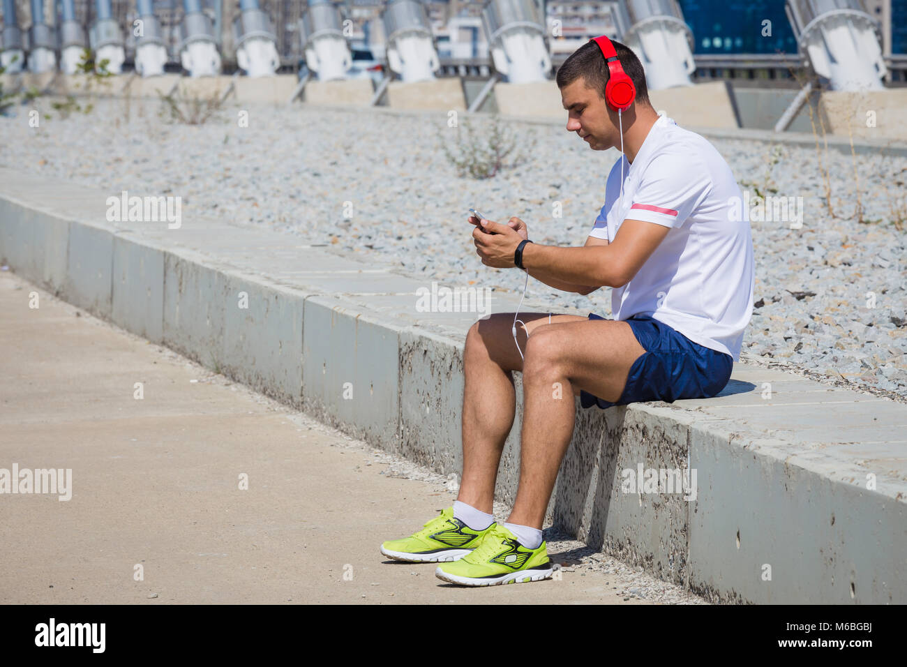 Runner sitting and resting while using headphones and smart phone ...