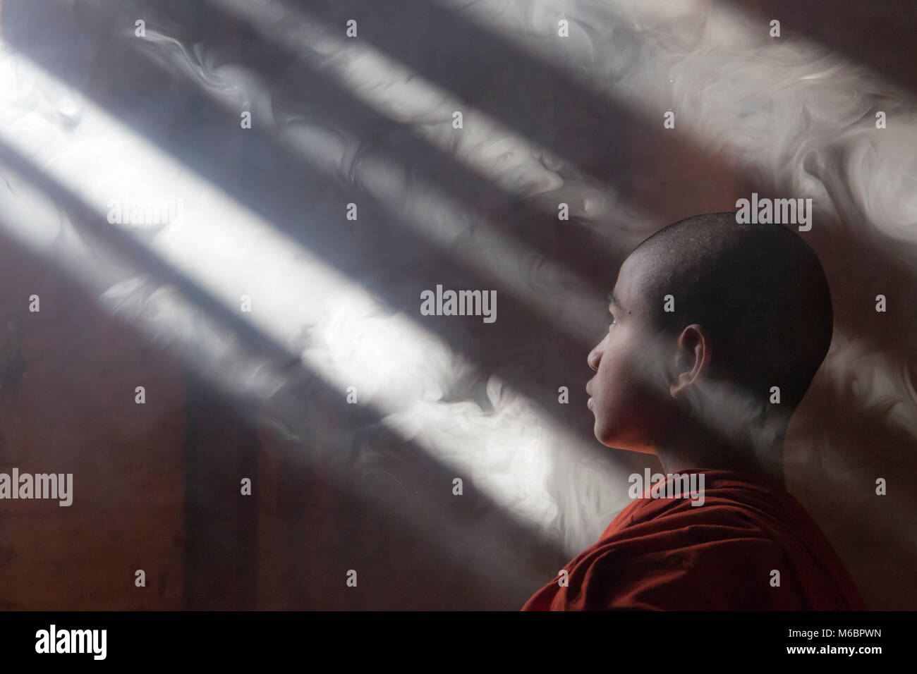 Face of novice Buddhist monk lit by shafts of sunbeams and smoke at ...