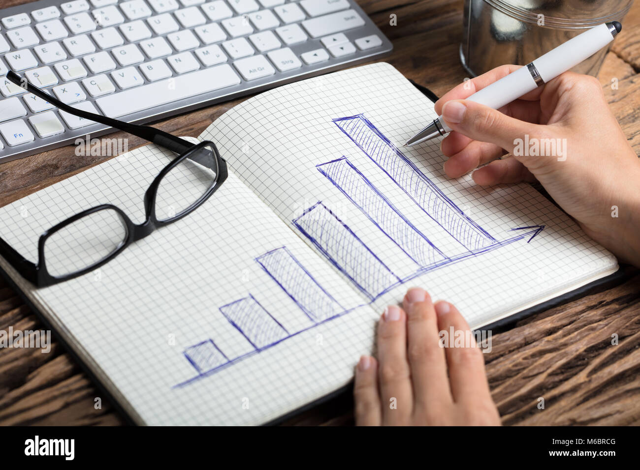 Close-up Of A Businessperson's Hand Drawing Graph With Pen On Notebook ...