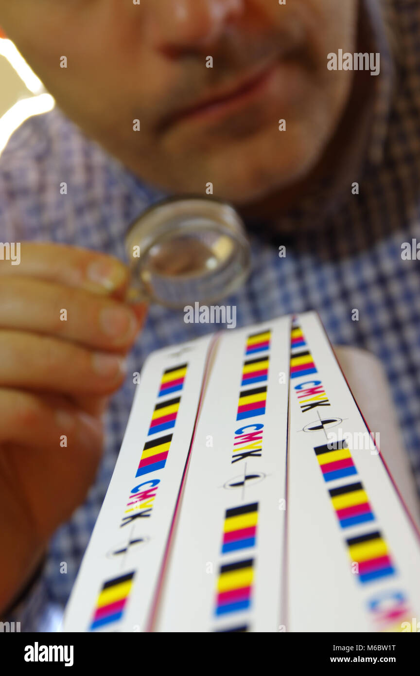 Printer looking at test cmyk registers on paper using magnifier. Man ...
