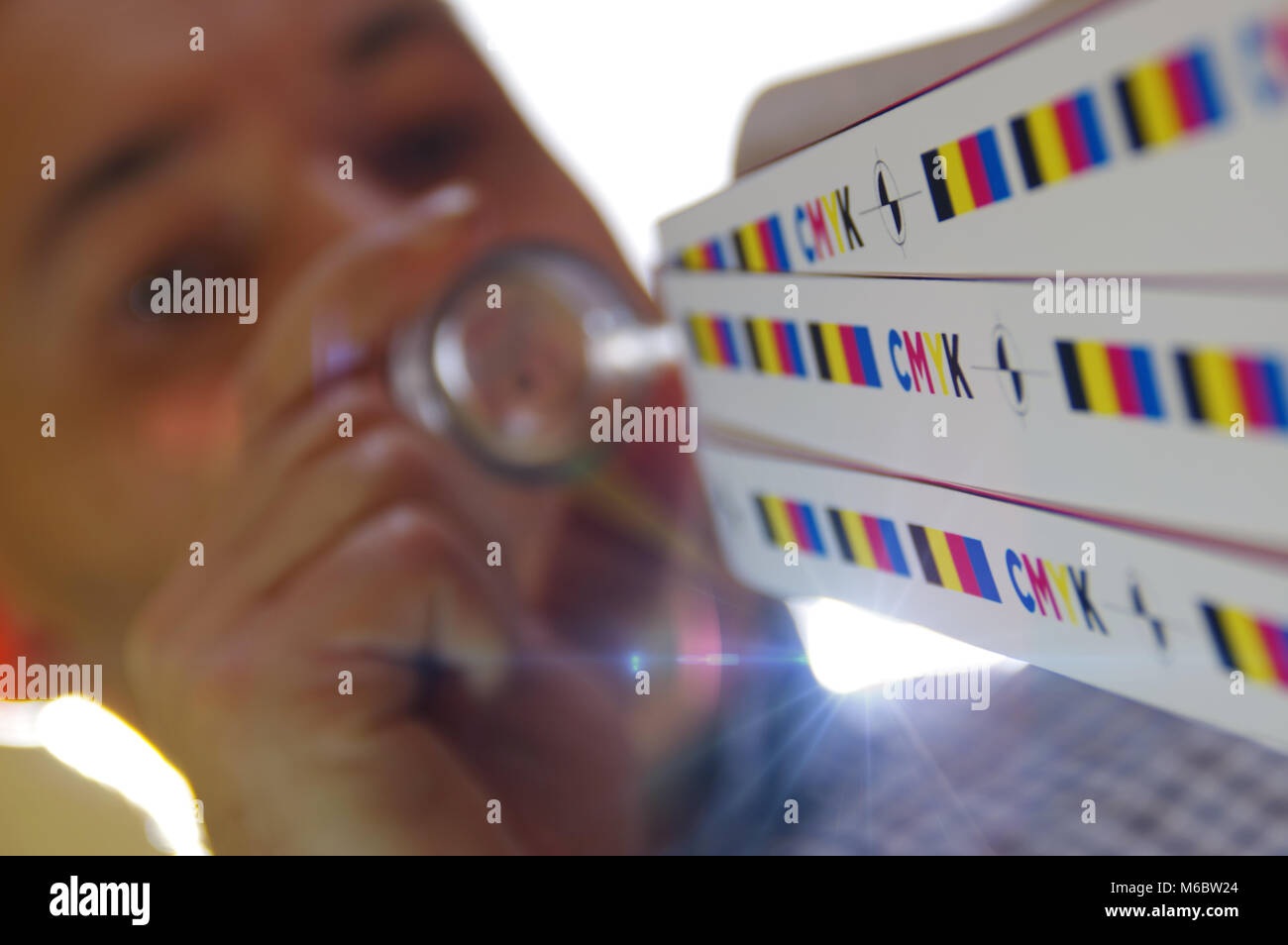 Printer testing cmyk registers on paper using magnifier. Man checking ...