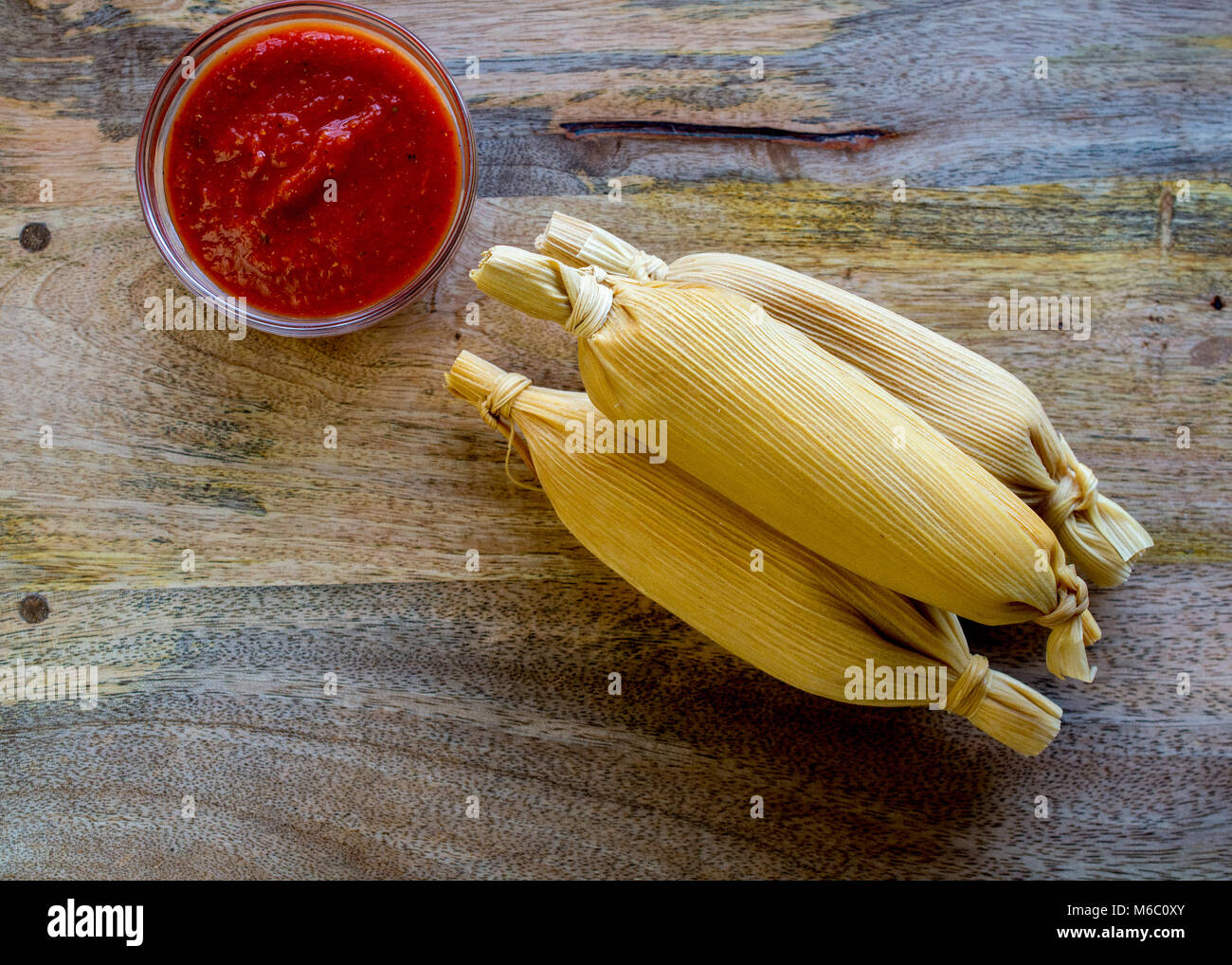 Three whole, wrapped tamales on wooden table served with hot tomato ...