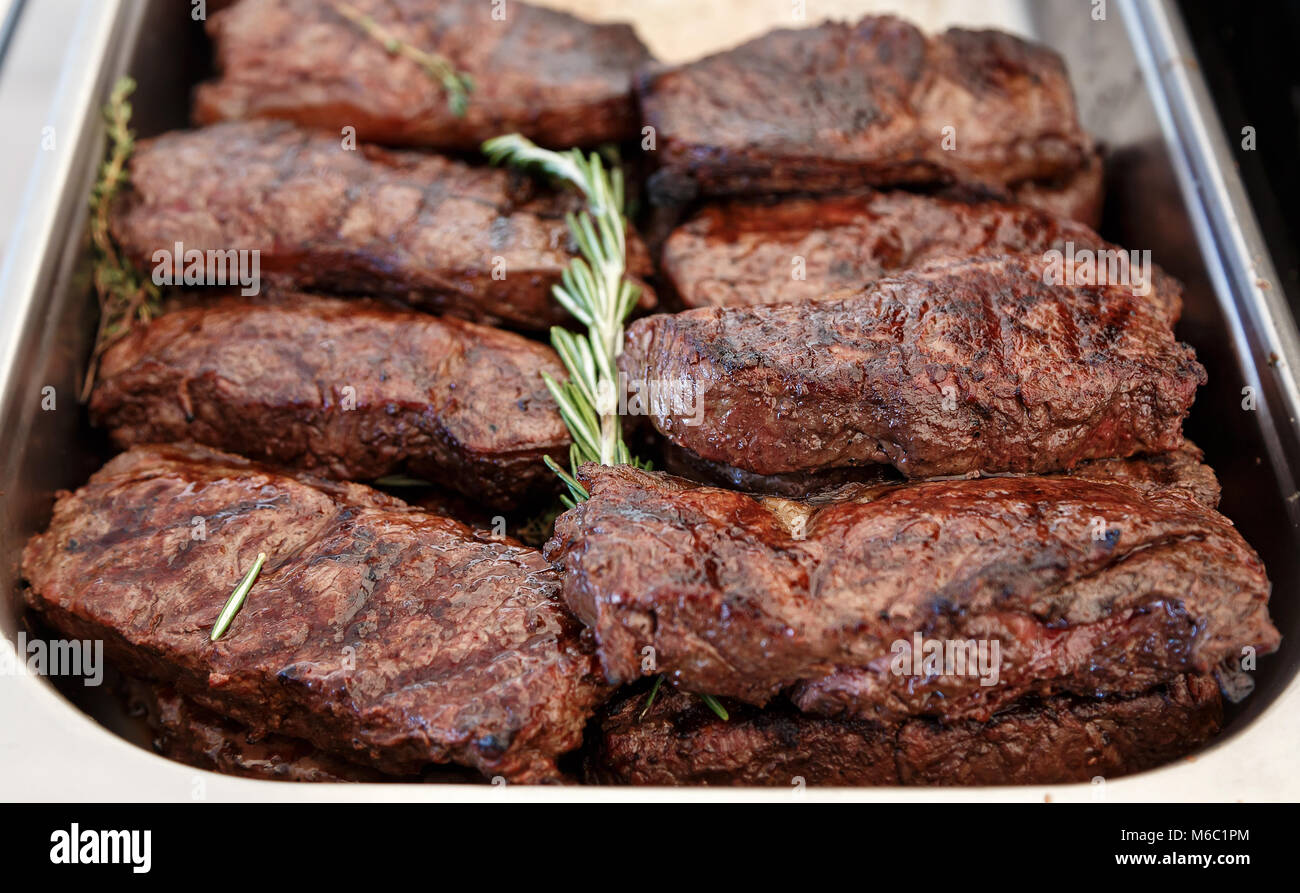 A lot of cooked veal steaks rib eye. On the steaks lies a branch of ...