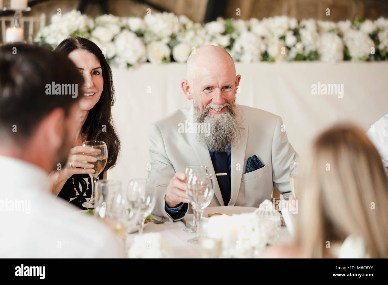 A table of happy wedding guests are socialising as they eat the ...