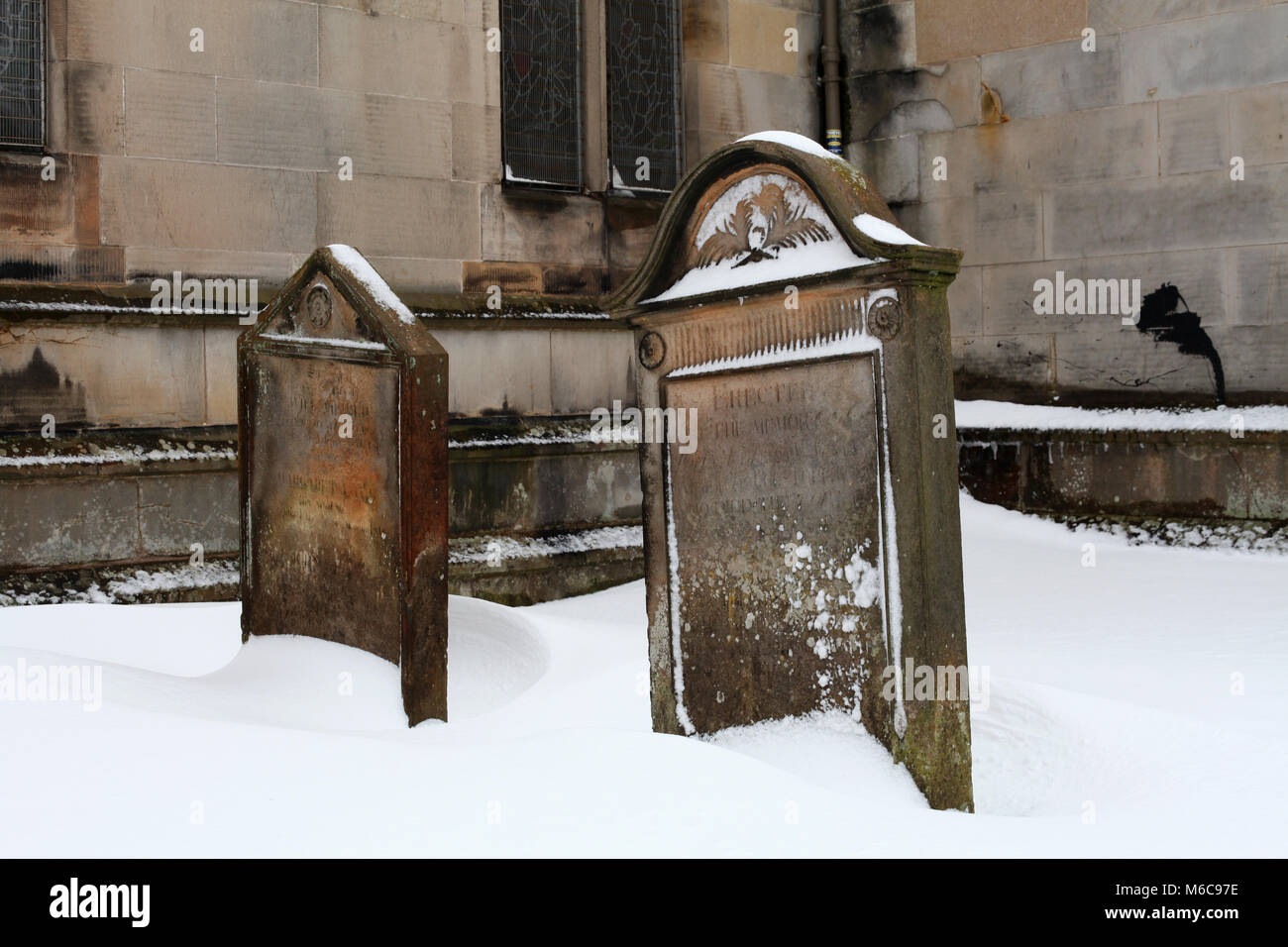 Two gravestones partially covered by drifting snow in the grounds of ...